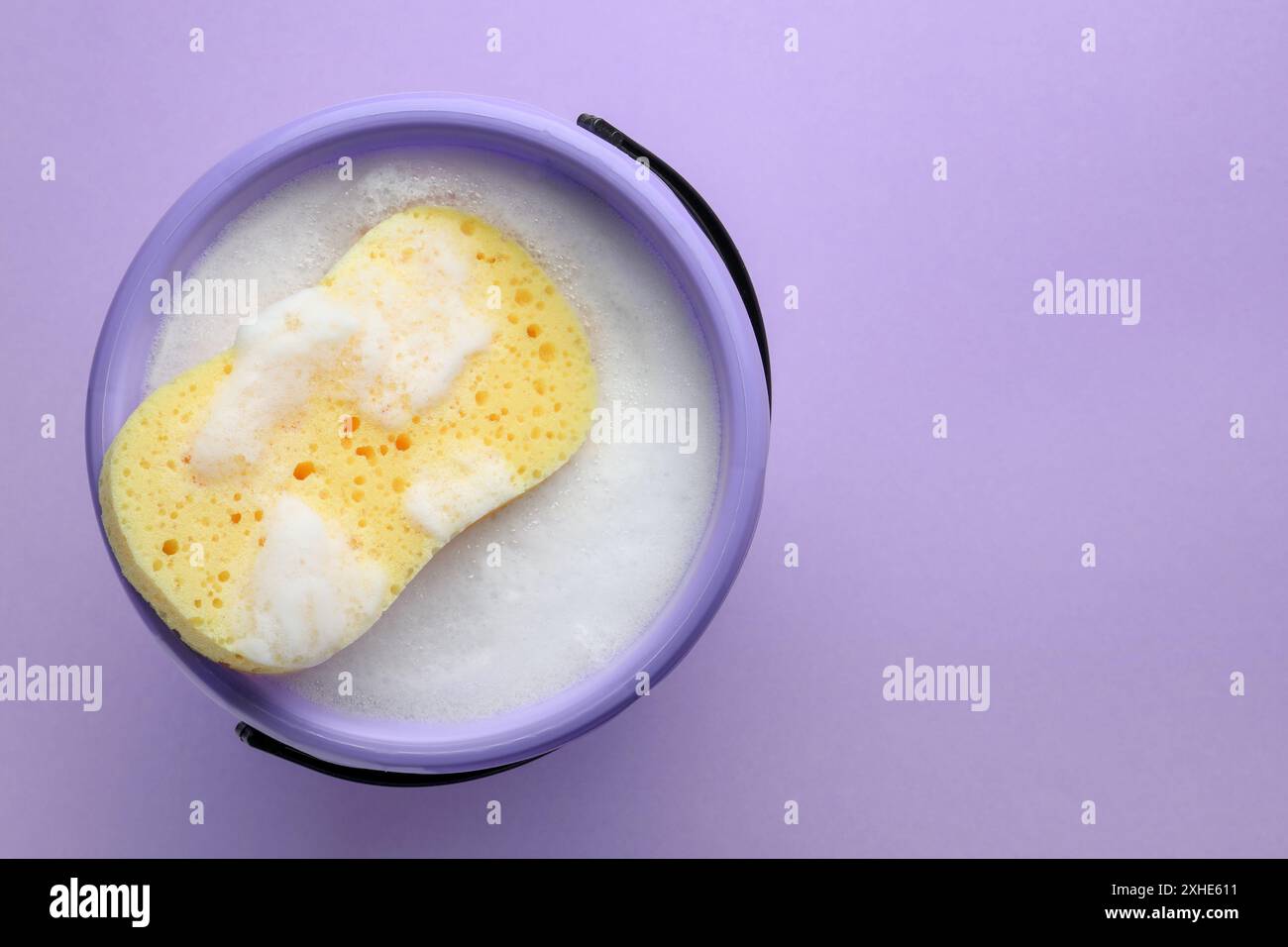 Bucket with foam and sponge on violet background, top view. Space for ...