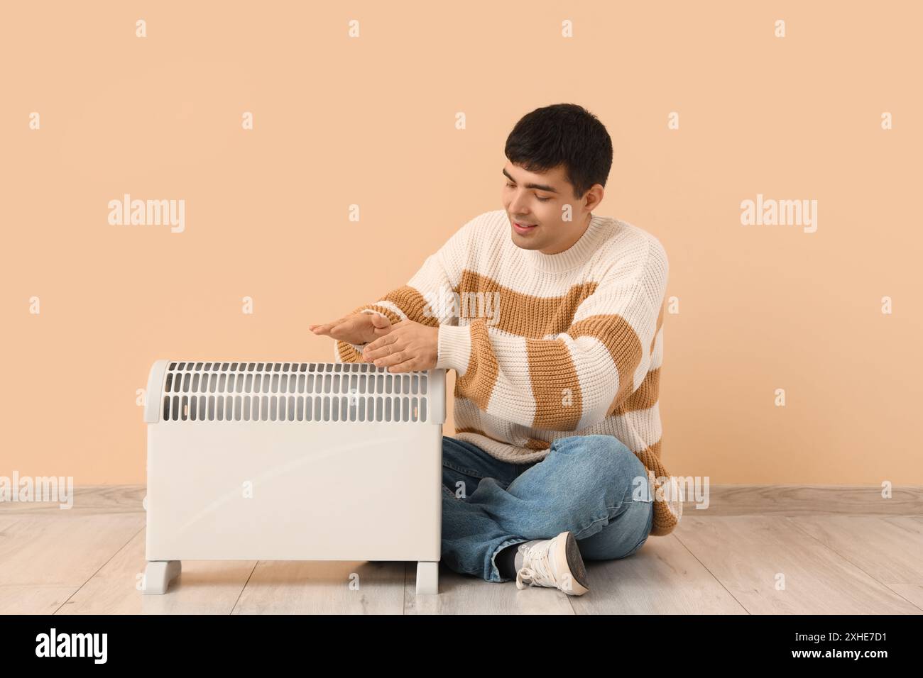 Frozen young man with radiator sitting near beige wall Stock Photo - Alamy