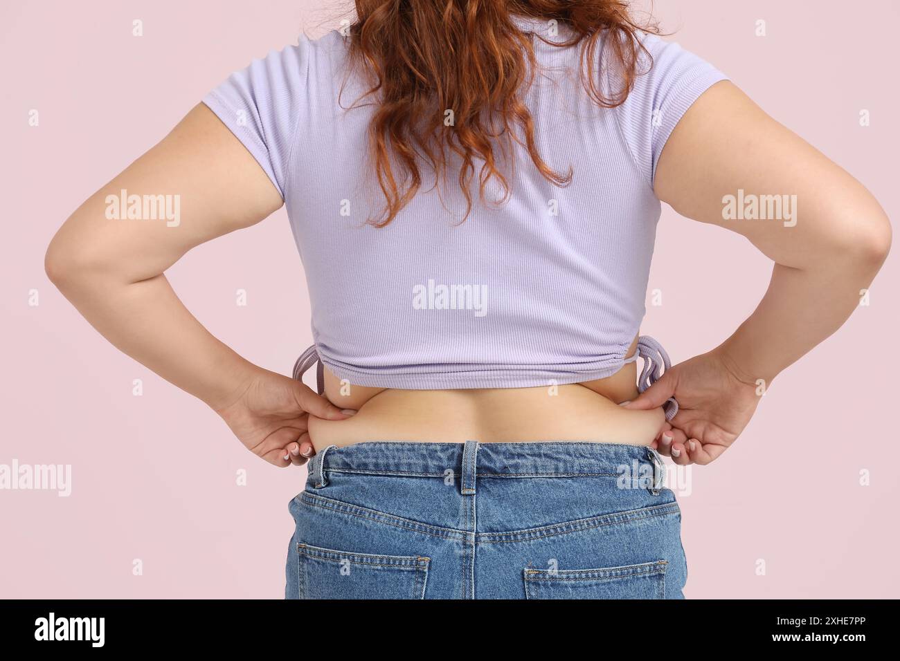 Overweight woman in tight jeans on pink background, back view. Excess ...