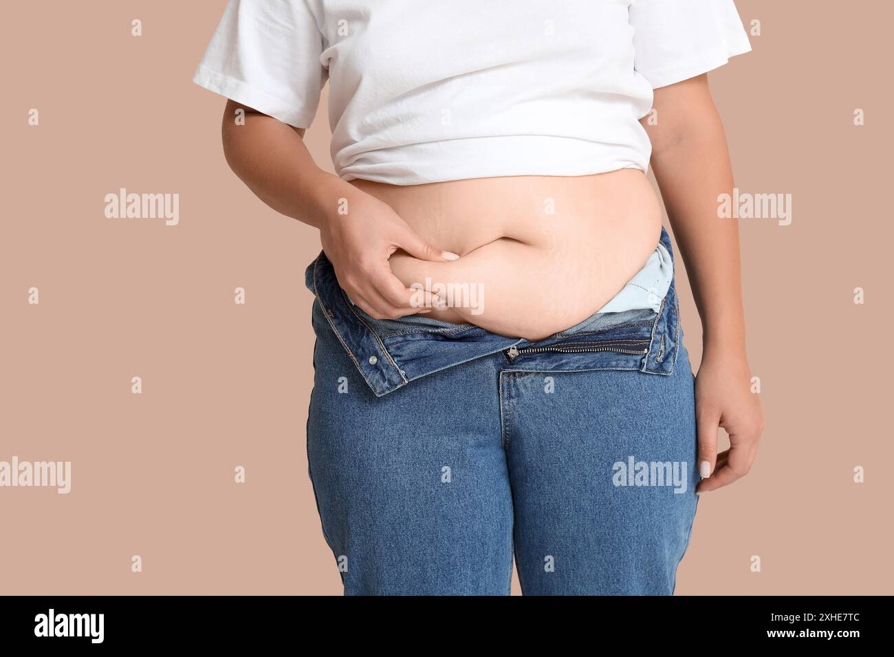 Overweight woman in tight jeans on beige background. Excess weight ...
