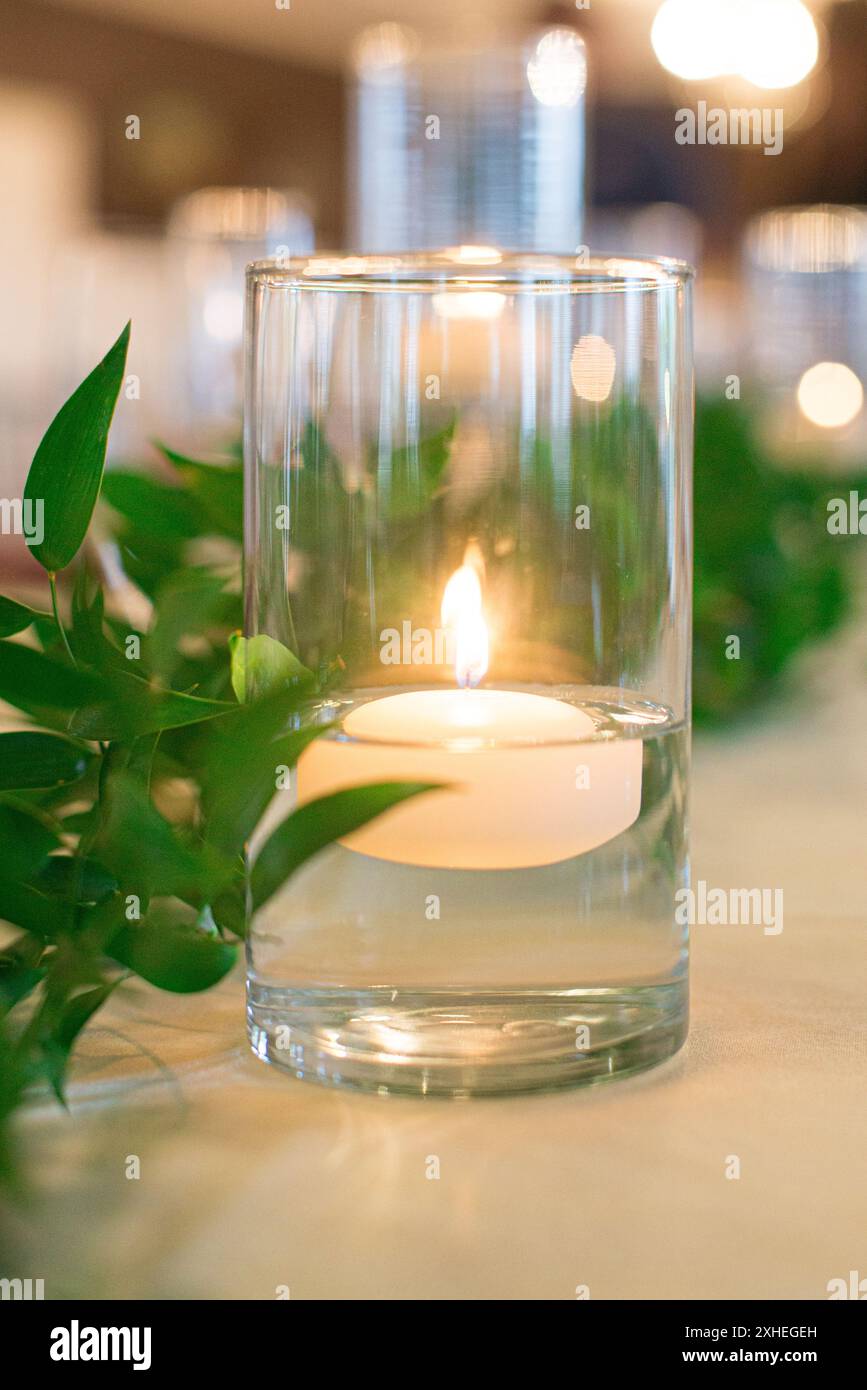 Tall glass vase with lit tea light candle floating inside on wedding ...