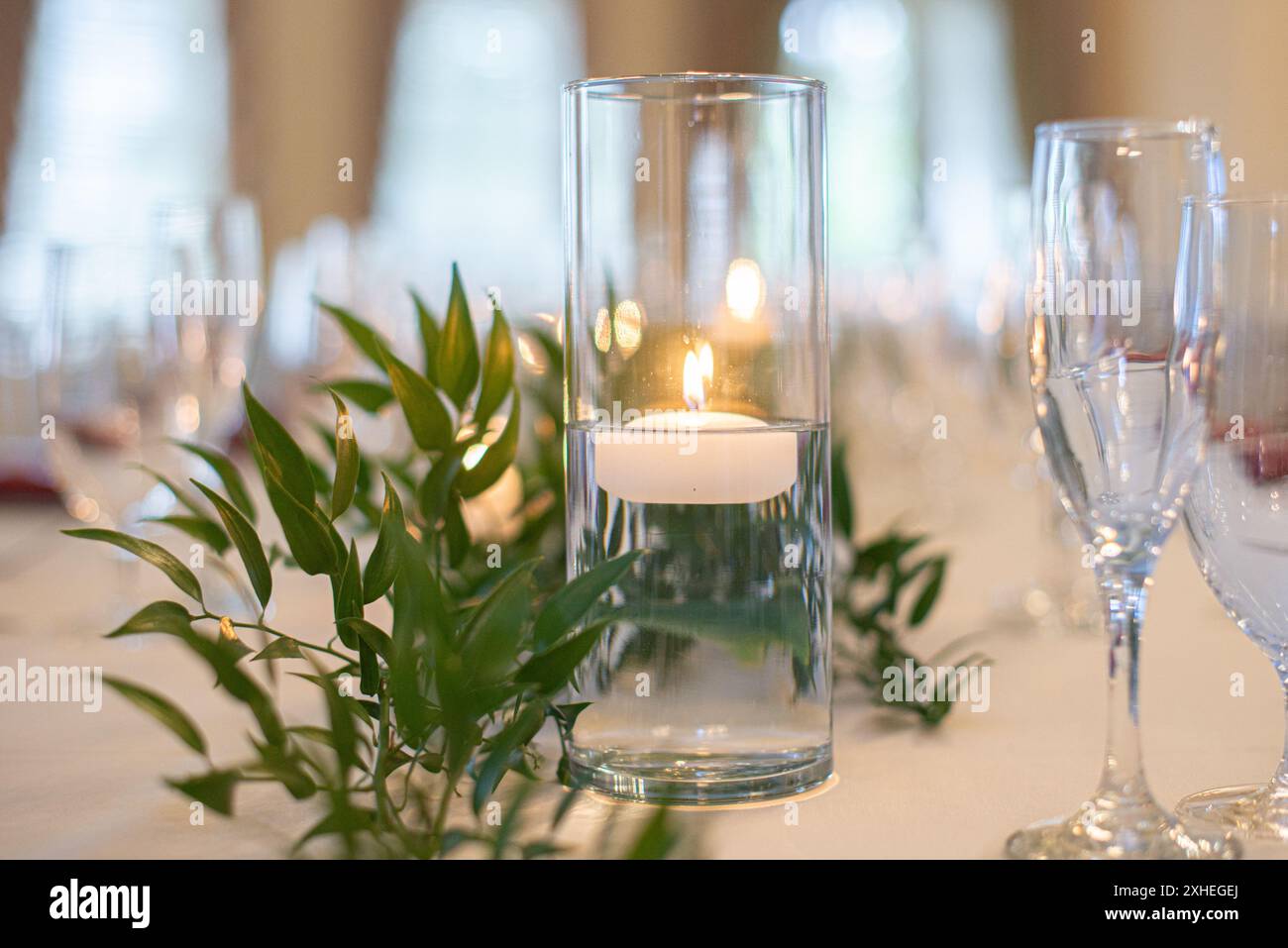 Tall glass vase with lit tea light candle floating inside on wedding ...