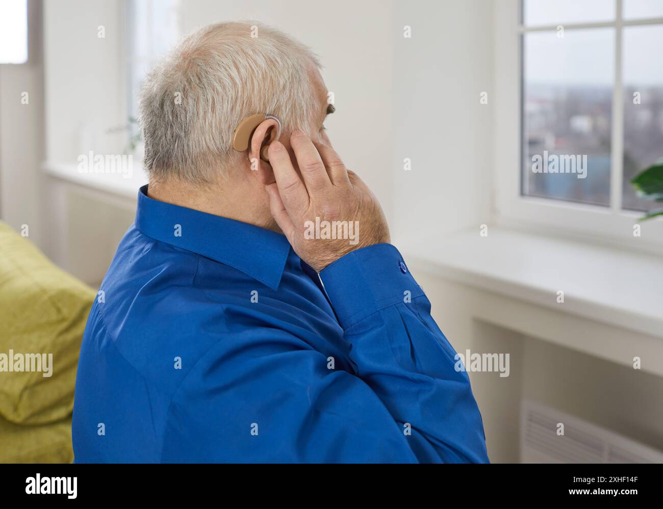 Side view of gray-haired senior man wearing modern hearing aid in his ...