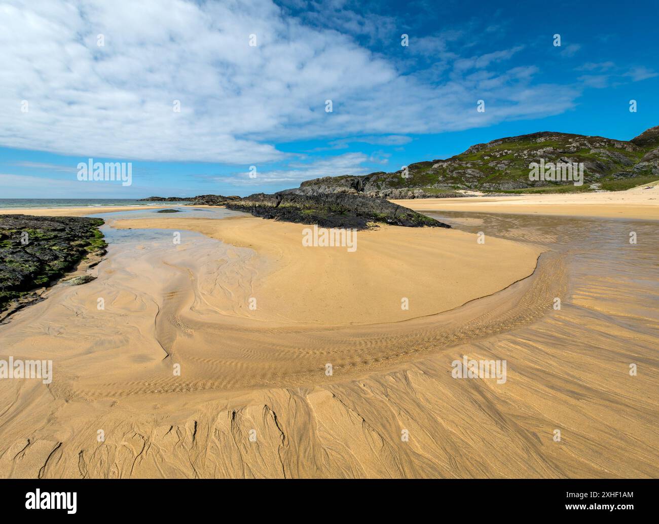 Pretty rivulet patterns in the yellow sand of Kiloran beach with blue ...