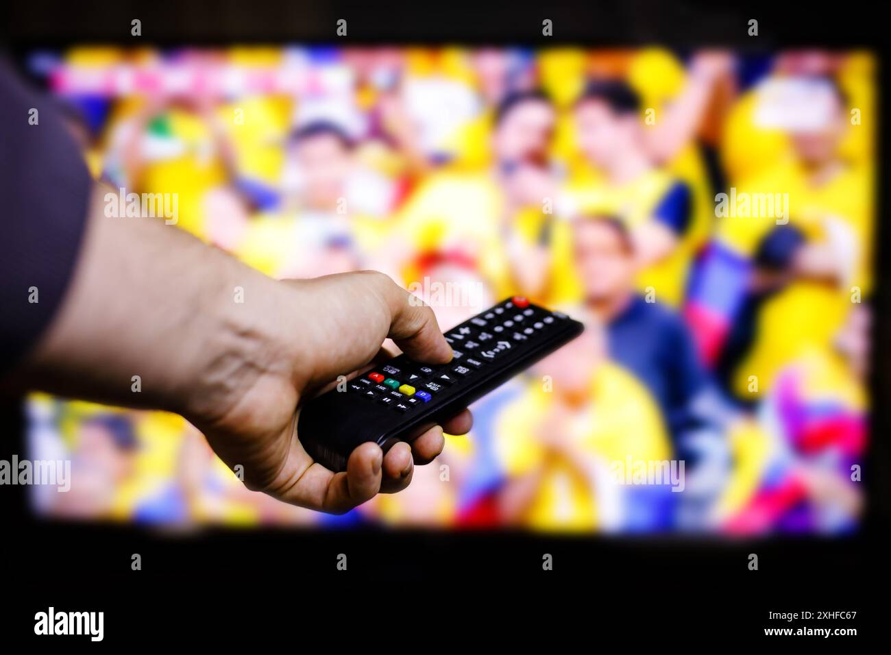 A person's hand holds a television remote control in front of a ...