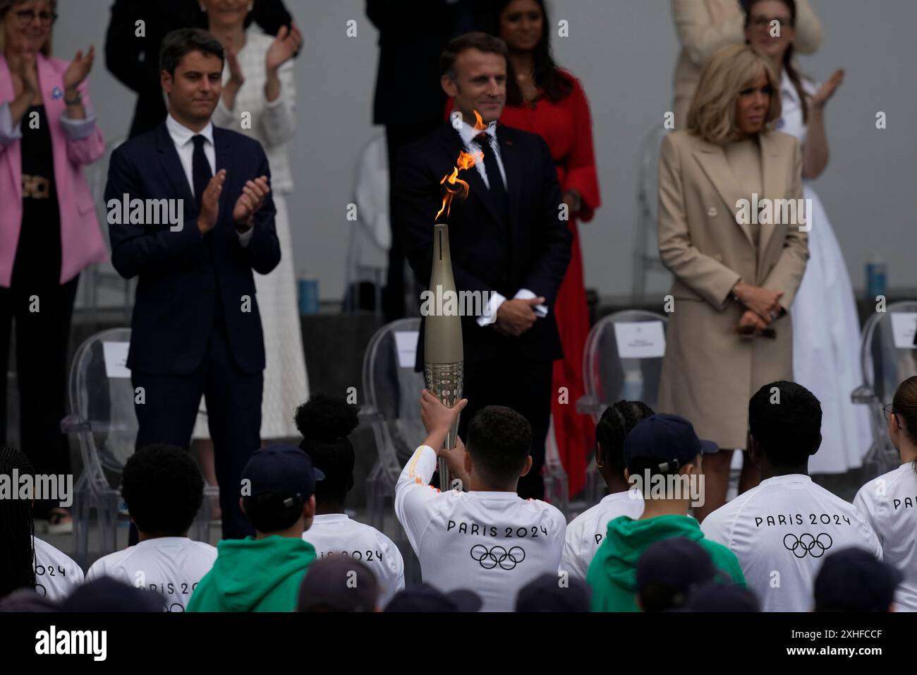 The Olympic torch is held by French President Emmanuel Macron, center ...