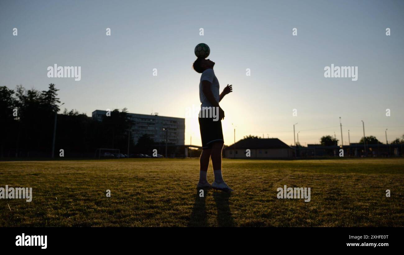 Professional footballer juggling soccer ball on stadium at sunset ...