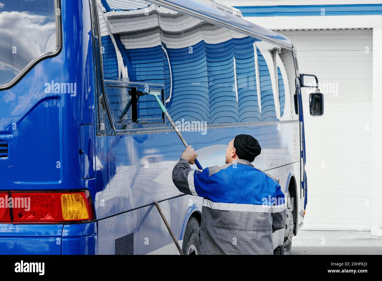 A diligent worker cleans bus windows with a mop, standing on the bus's ...