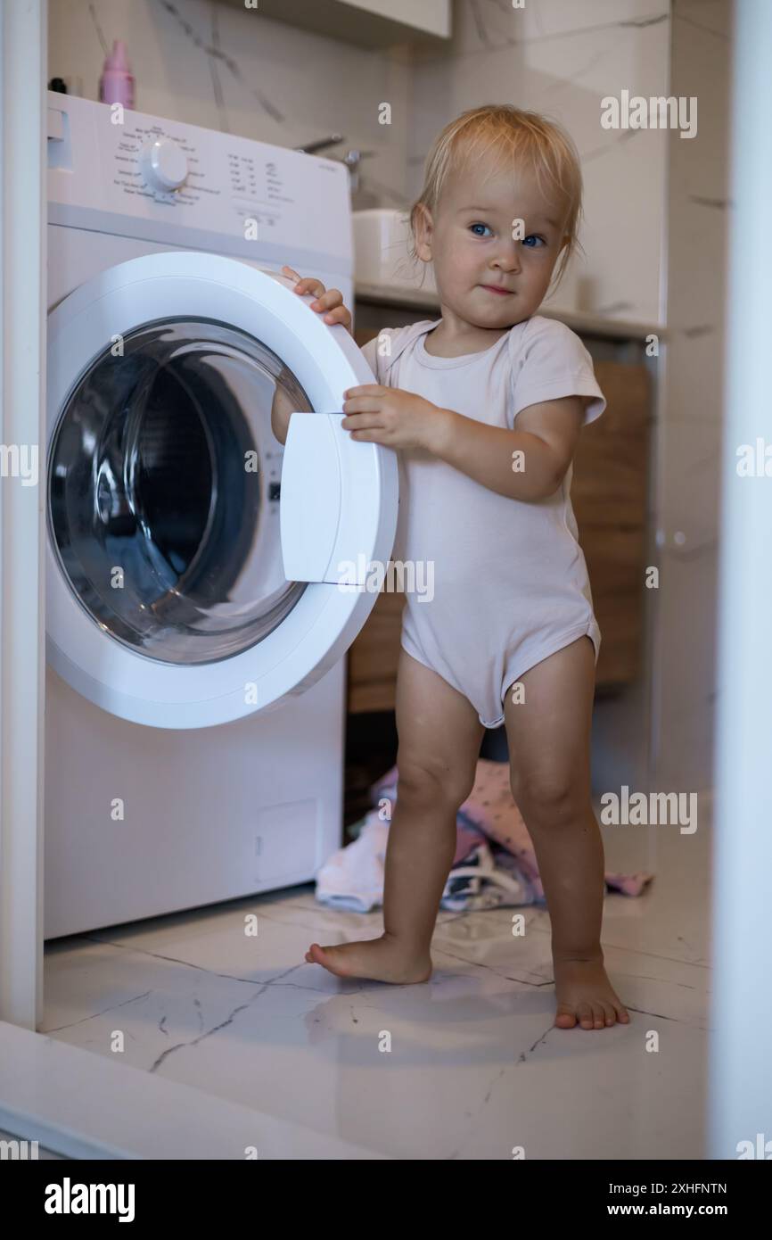 Two year old child doing household chores. Loading washing machine ...