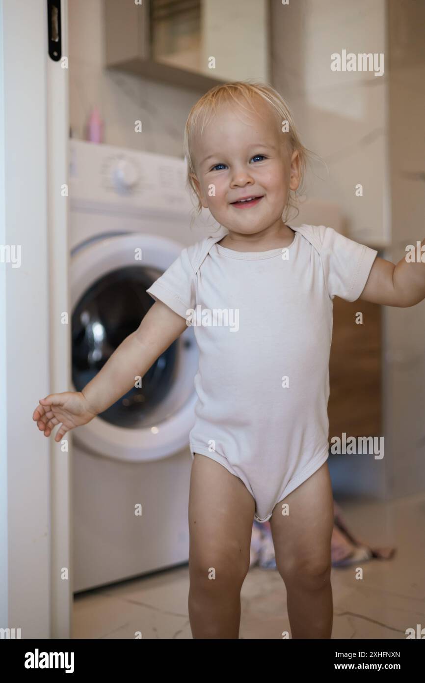 Two year old child doing household chores. Loading washing machine ...