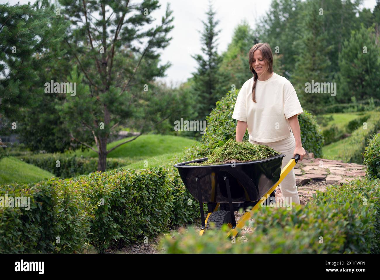 Woman gardener pushing wheelbarrow filled with plants through green ...