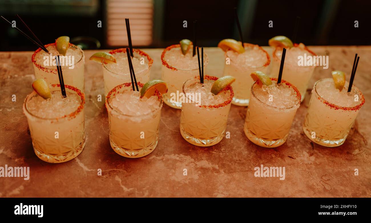 A row of refreshing cocktails garnished with lime wedges and chili salt ...