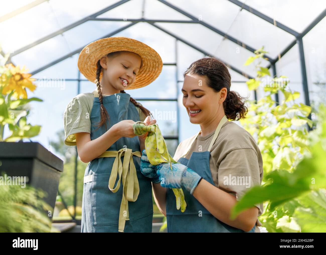 Happy mother and daughter are gardening in the greenhouse. Child is ...
