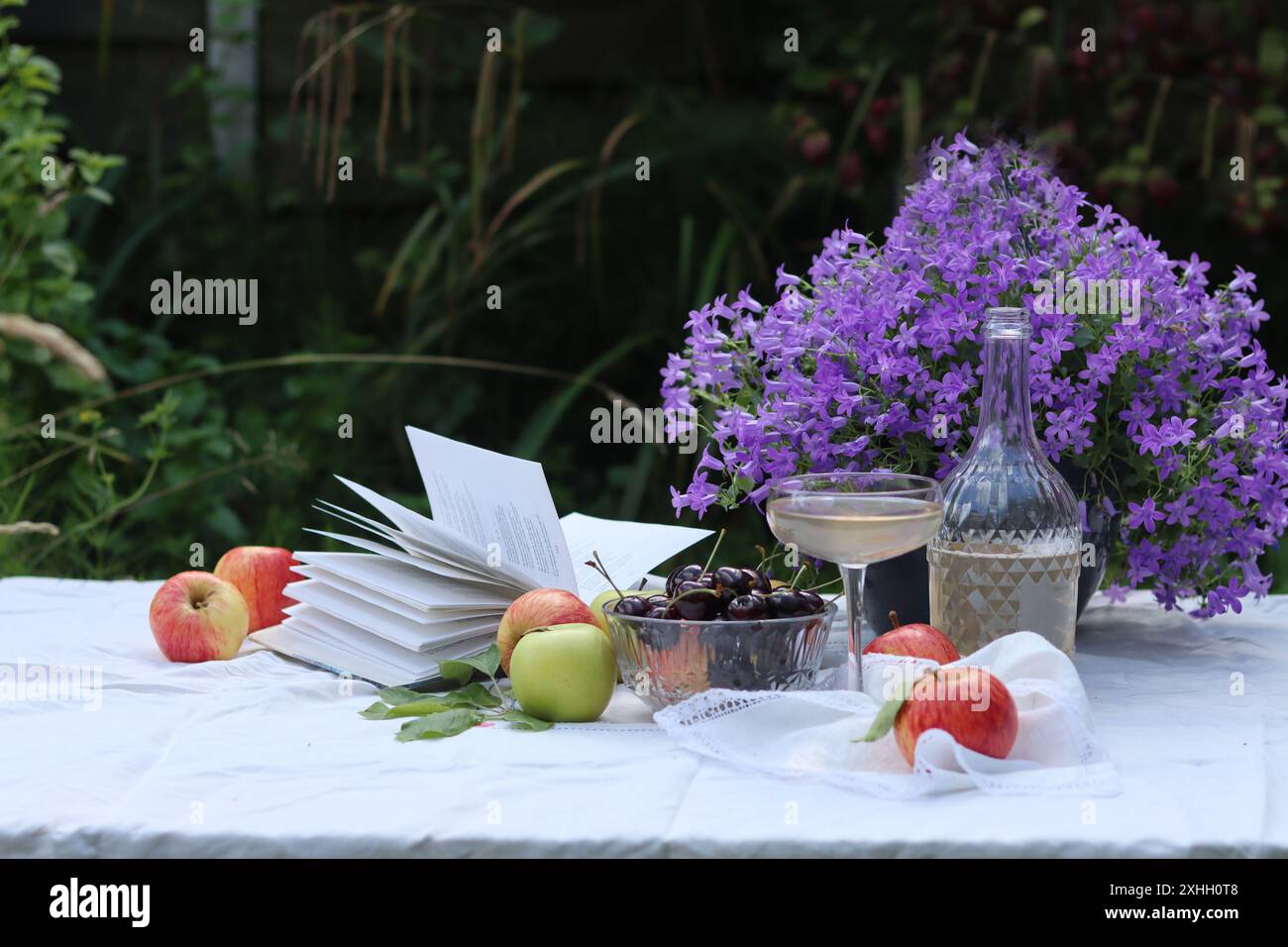Picnic table with wine, apples, cherry and flowers in the summer garden ...