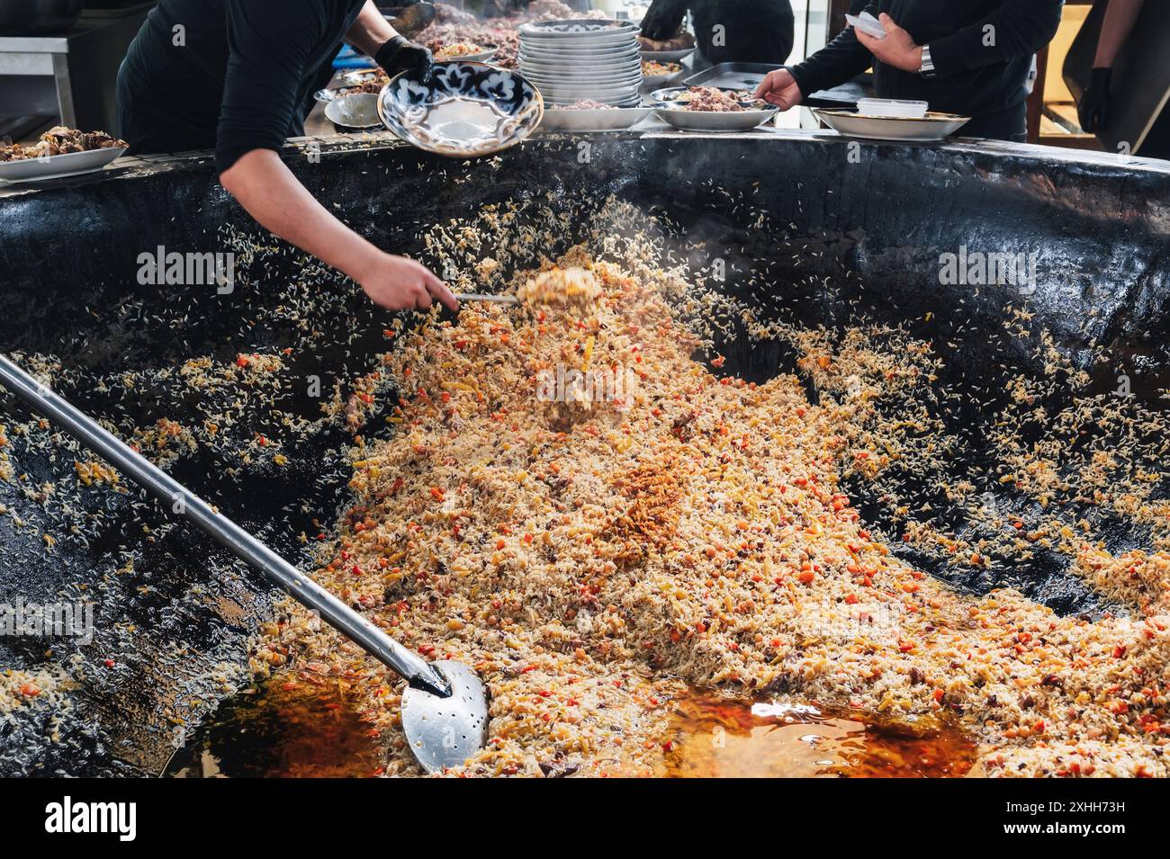 cooking traditional oriental Uzbek pilaf in a huge cauldron in the ...