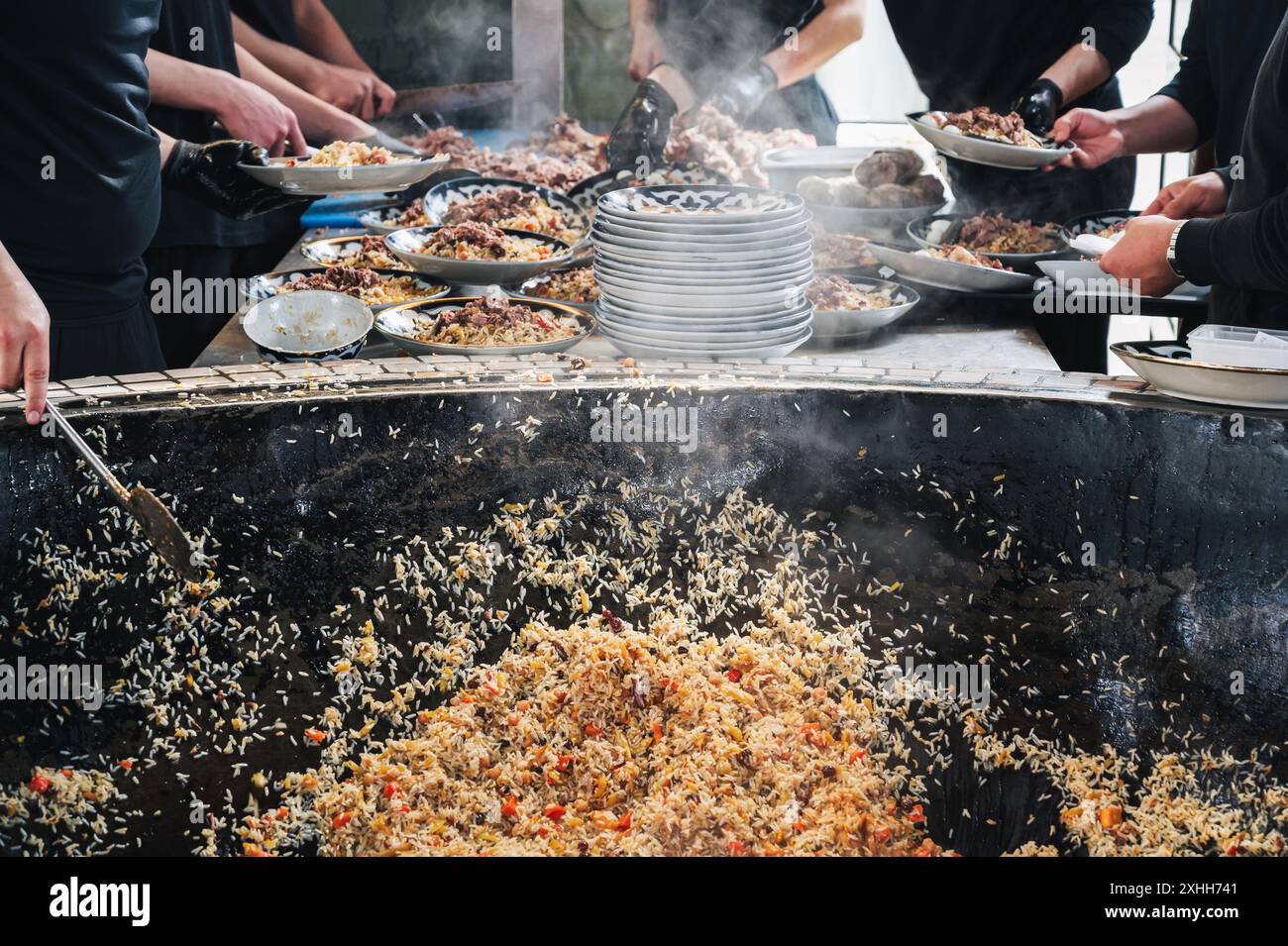 male chefs cook Uzbek rice pilaf with vegetables in cauldron in the ...