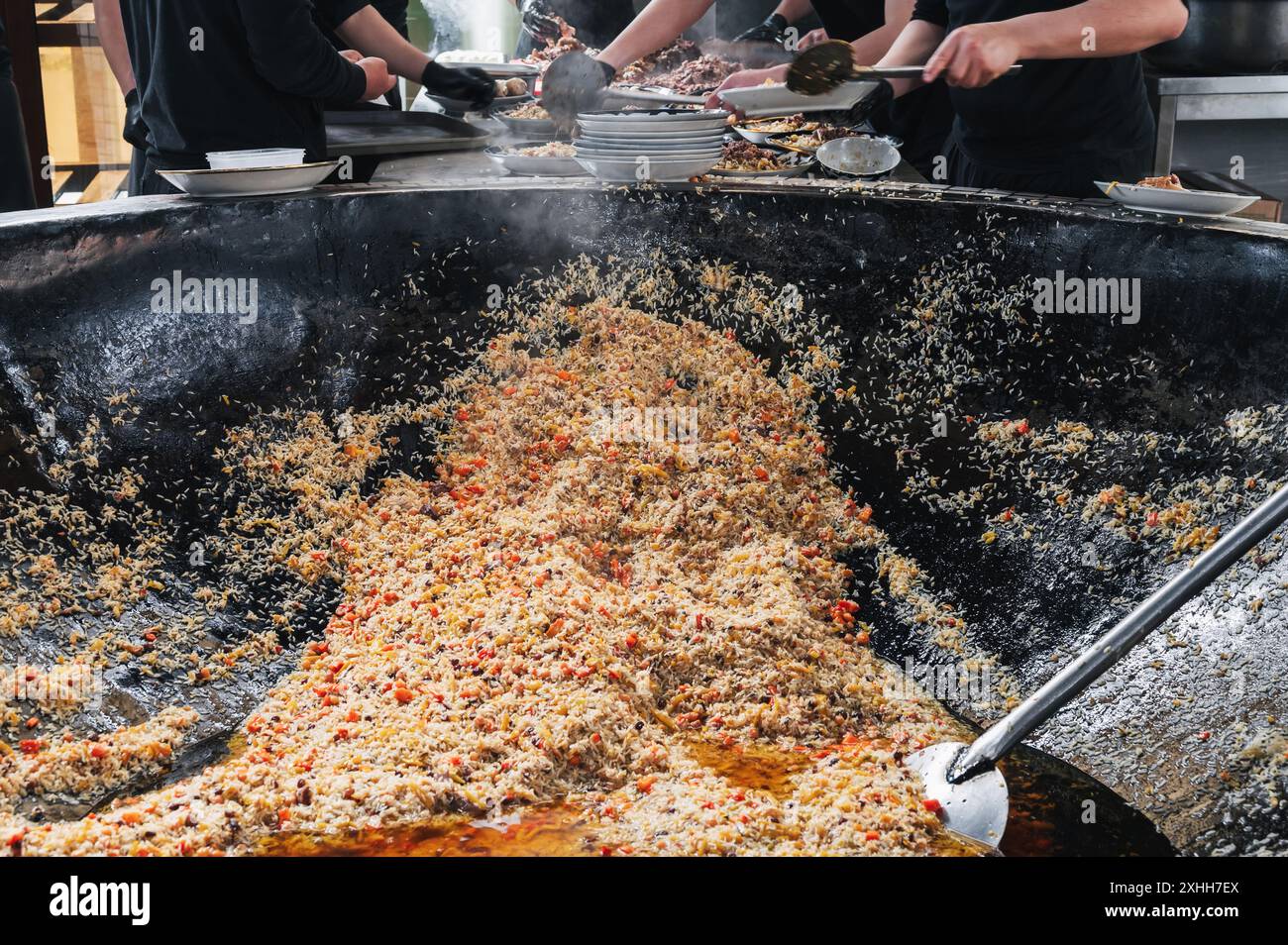 hands male chefs cook Uzbek rice pilaf in a big cauldron in the kitchen ...