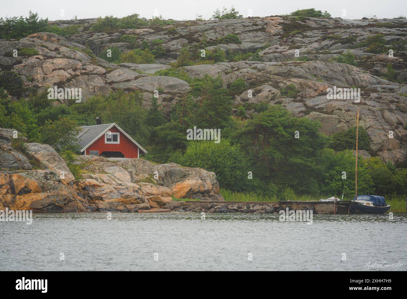 In a serene setting, a red cabin sits in rocky hills and lush forest ...
