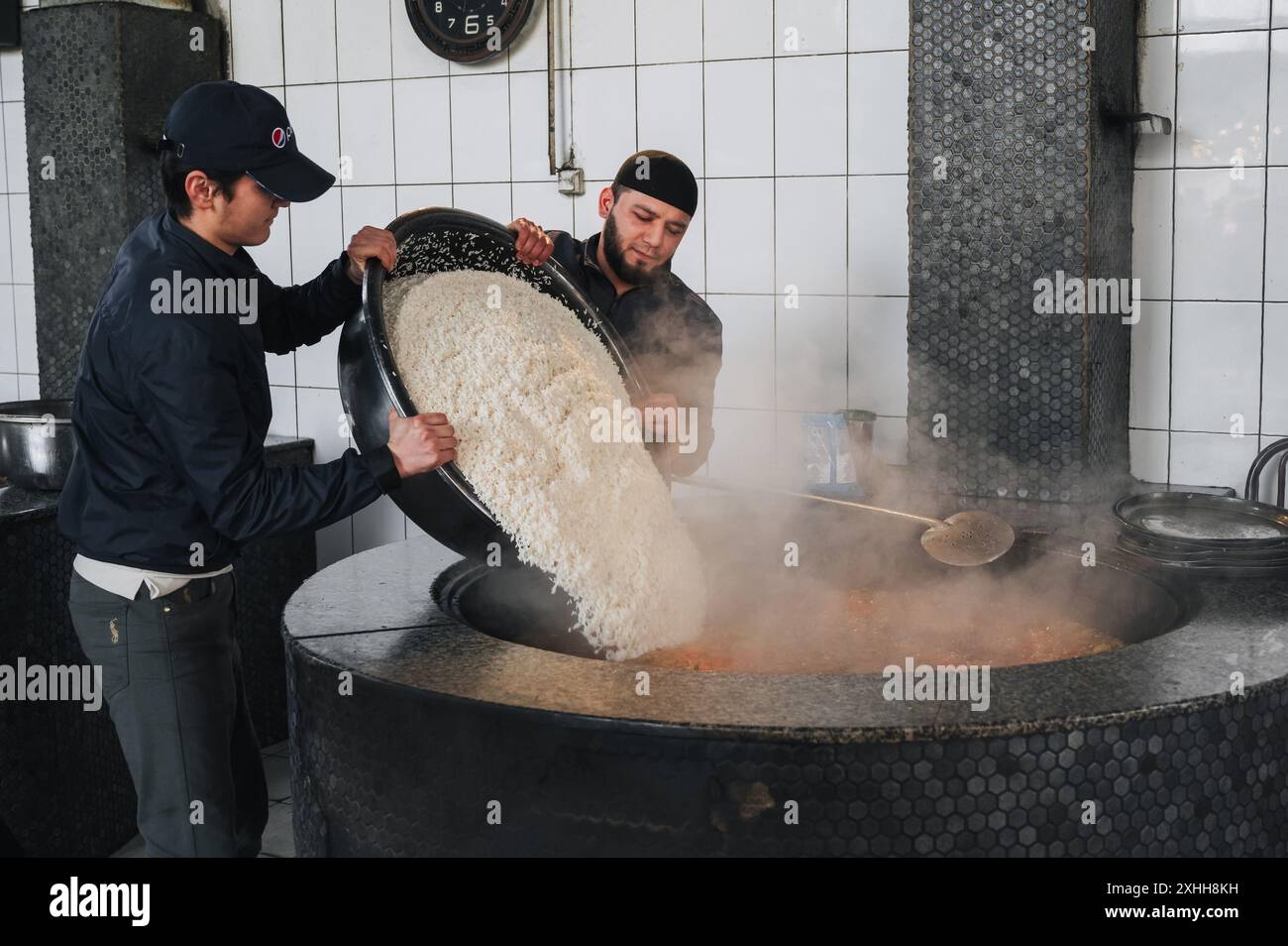 male chefs pour rice for traditional Uzbek pilaf into a cauldron in the ...