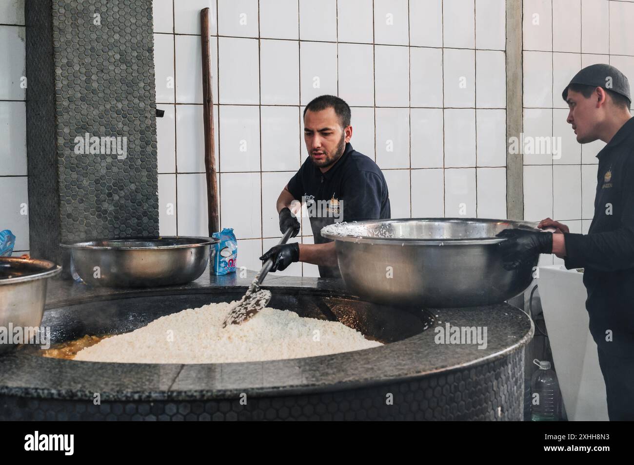 male cooks prepare rice for Uzbek pilaf in a cauldron in kitchen of a ...