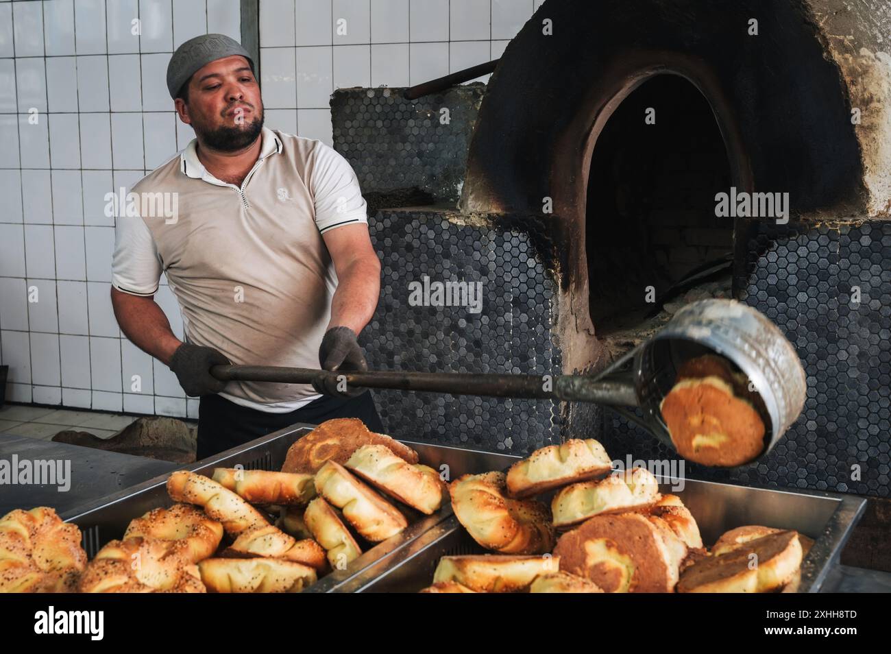 man baker bakes traditional bread Uzbek flatbread in a tandoor in ...