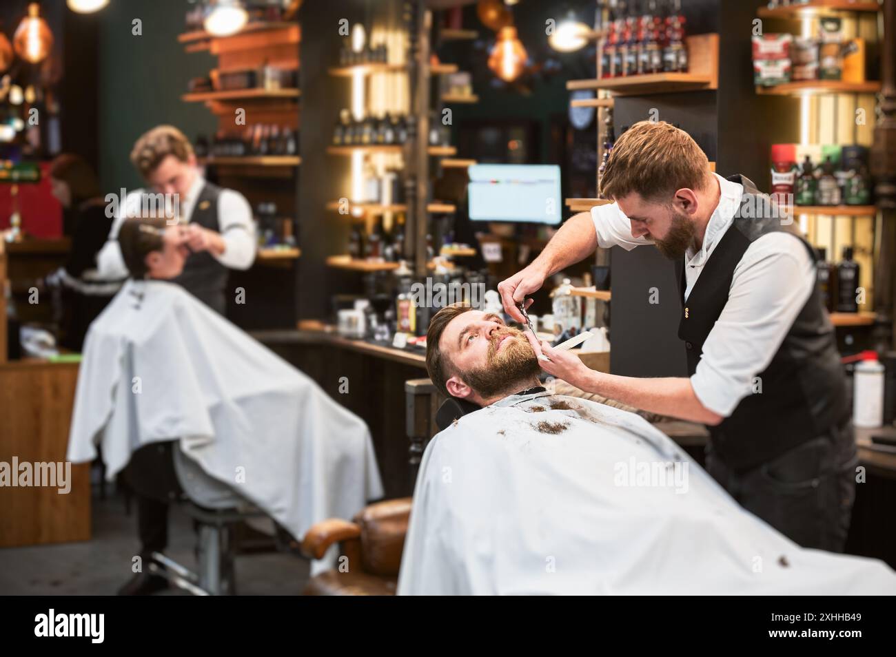 Busy day in modern barbershop. Professional barbers in fancy outfits at ...