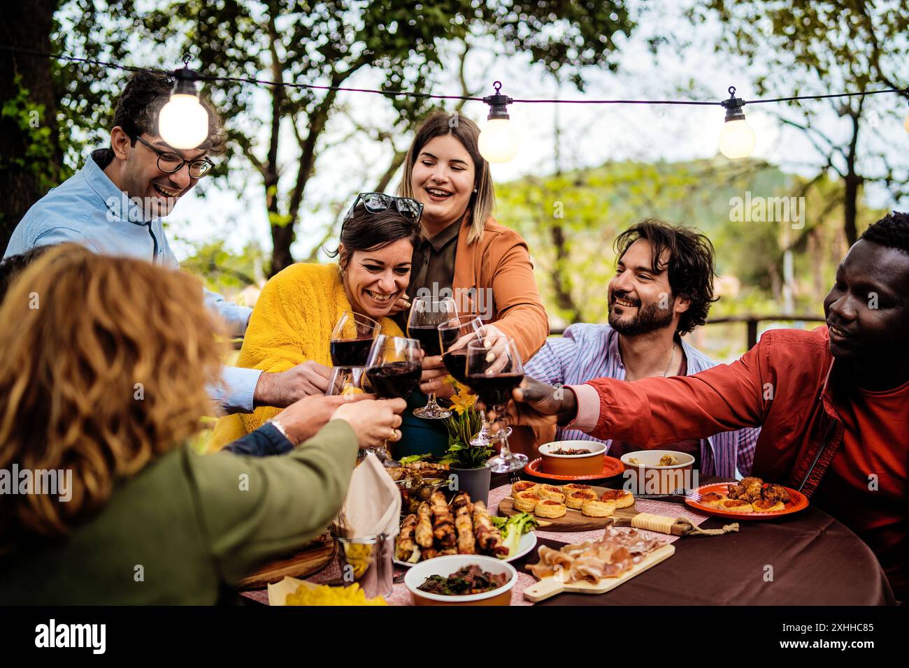 Joyful diverse group of friends toasting with wine at outdoor dinner ...