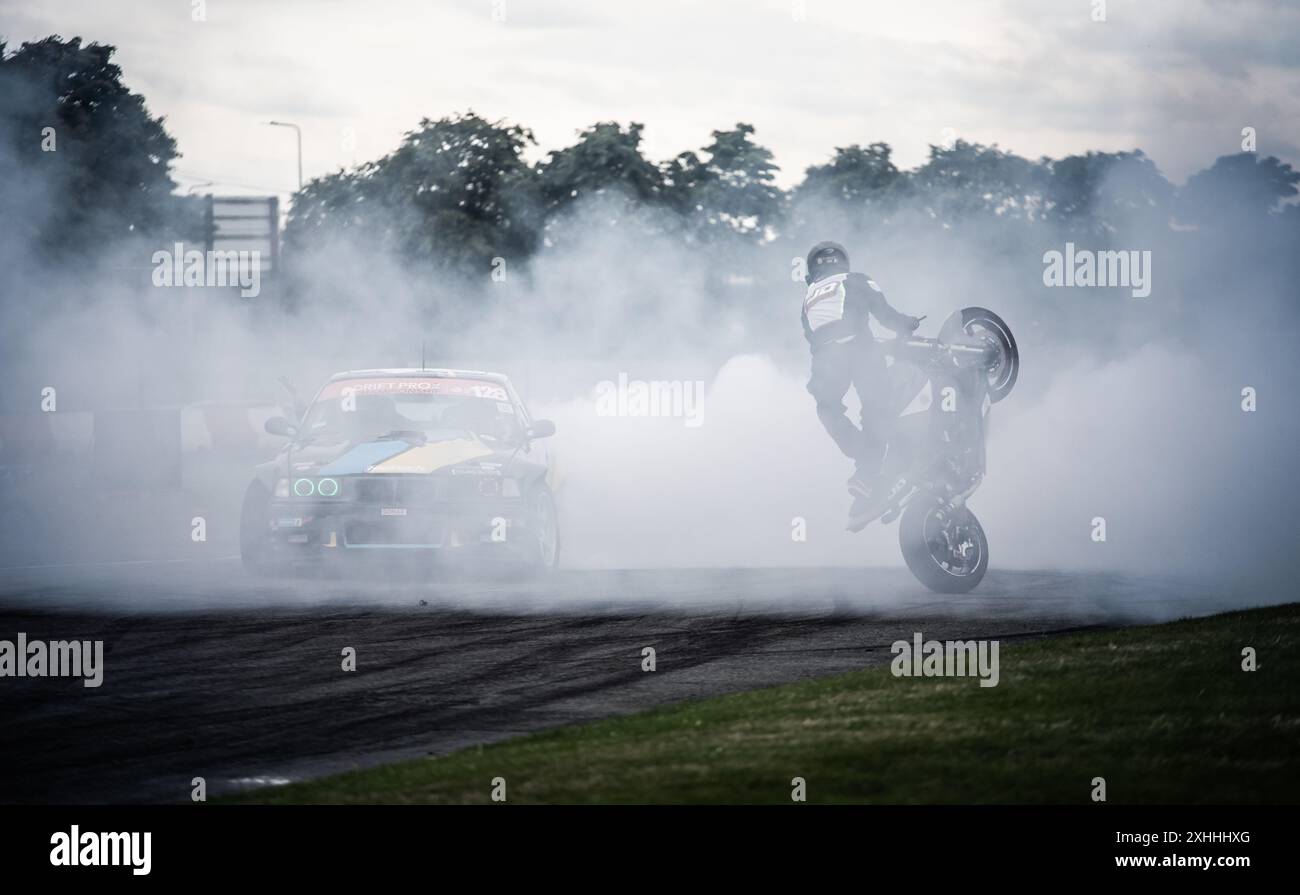 A Car Drifting Around a Motorbike Doing a Wheelie Stock Photo - Alamy
