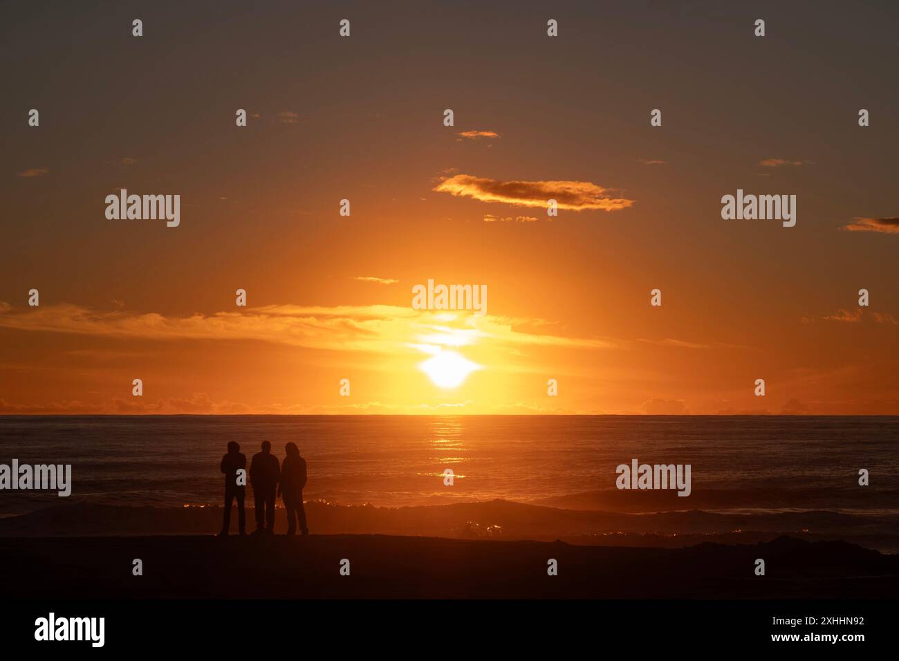 Silhouette of three people watching a golden California sunset over the ...