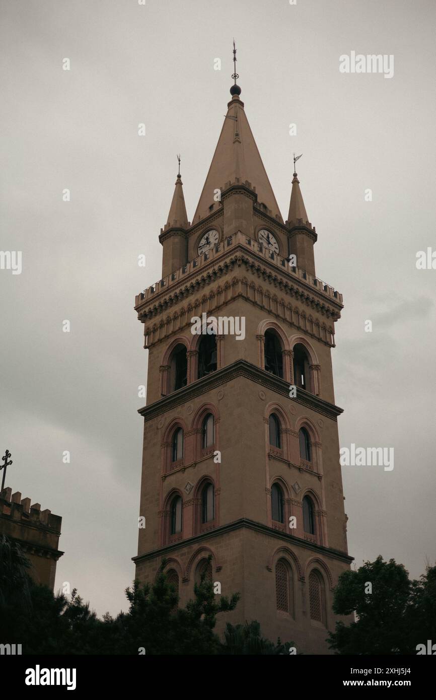 A tall clock tower with a pointed roof under a cloudy sky, surrounded ...