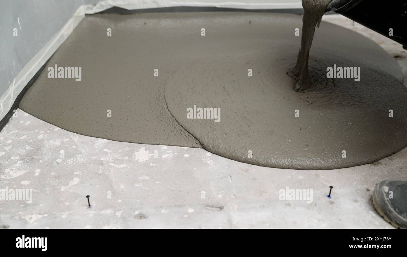 Workers pour solution from a bucket over the concrete floor. The ...