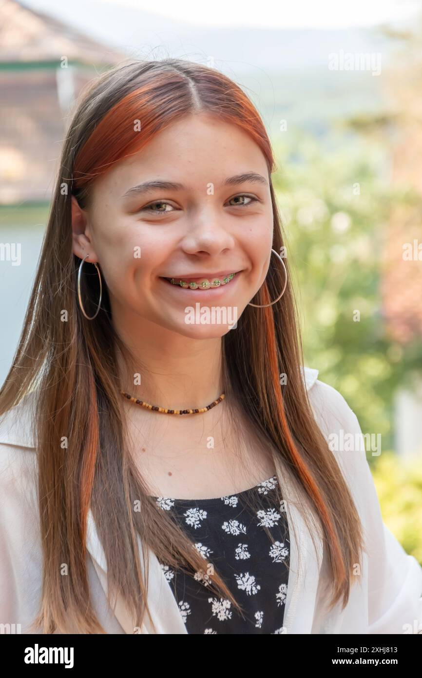 A long-haired teenage girl with braces smiles and looks at the camera ...