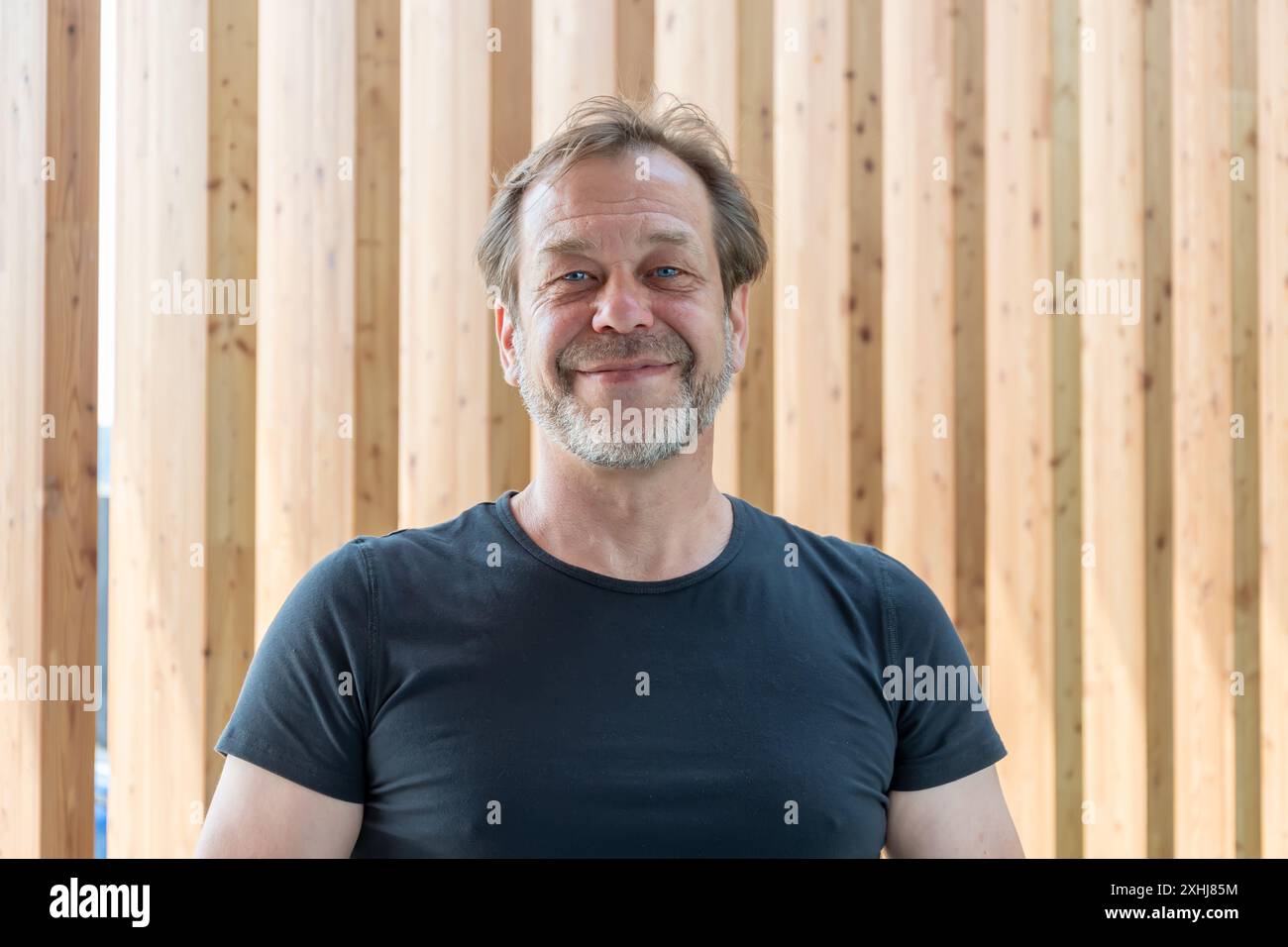 An elderly man 50-55 years old with a grey beard smiles in front of a ...