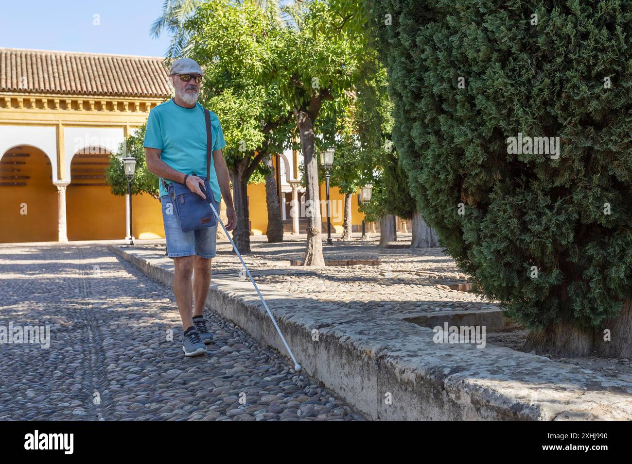 A mature blind man uses a white cane to guide himself through a ...