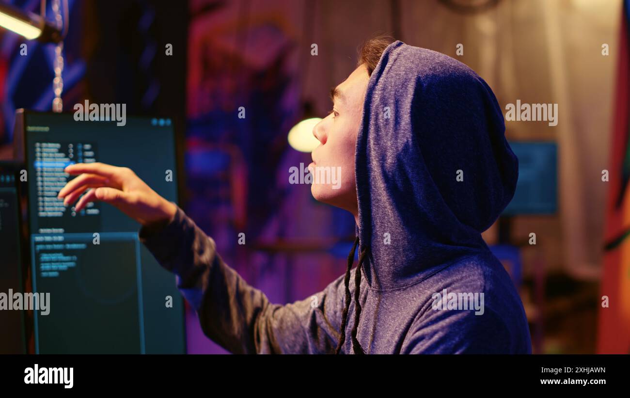 Hooded hacker talking with colleague while coding malware designed to exploit network backdoors ...