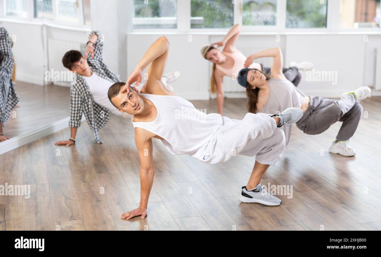 Man and his students perform hip hop dance on one bent leg, movement in ...