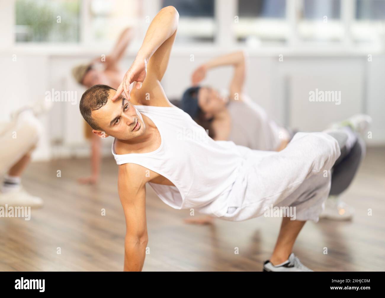 Man and his students perform hip hop dance on one bent leg, movement in ...