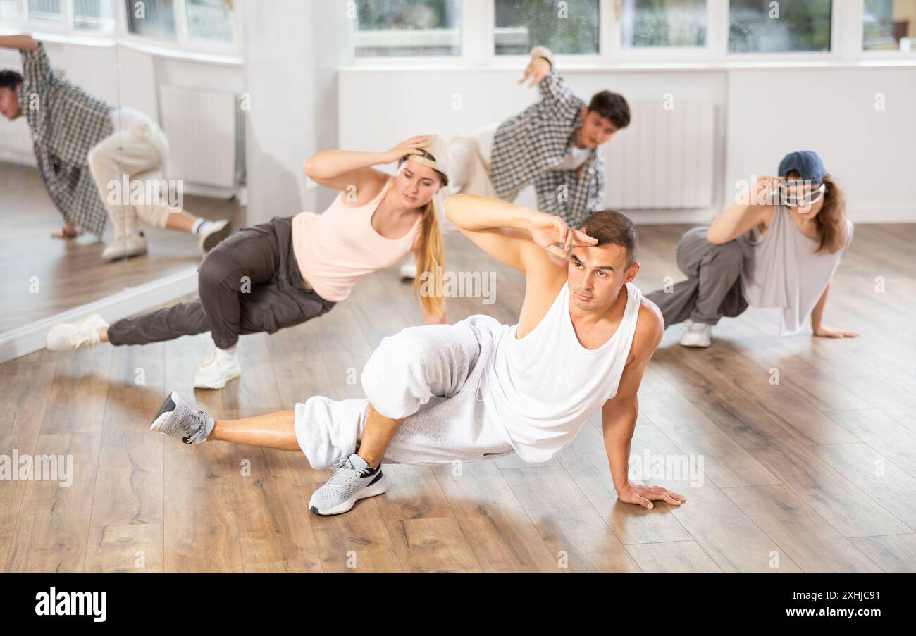 Man and his students perform hip hop dance on one bent leg, movement in ...