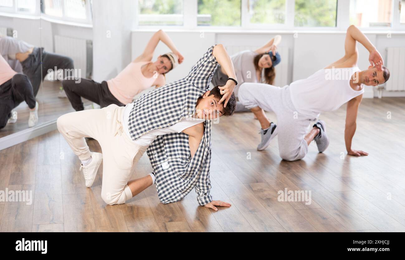 Man and his students perform hip hop dance on one bent leg, movement in ...