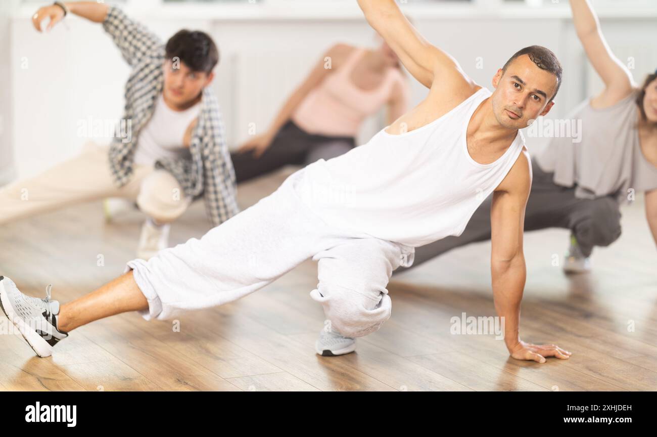Man and his students perform hip hop dance on one bent leg, movement in ...