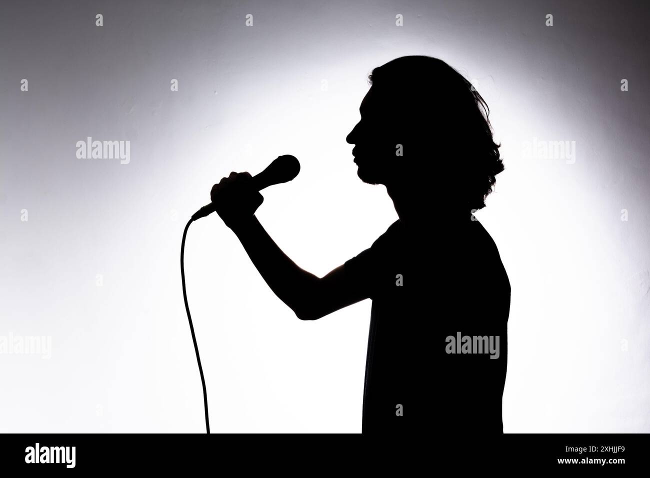 Silhouette of young singer holding wired microphone and singing with ...