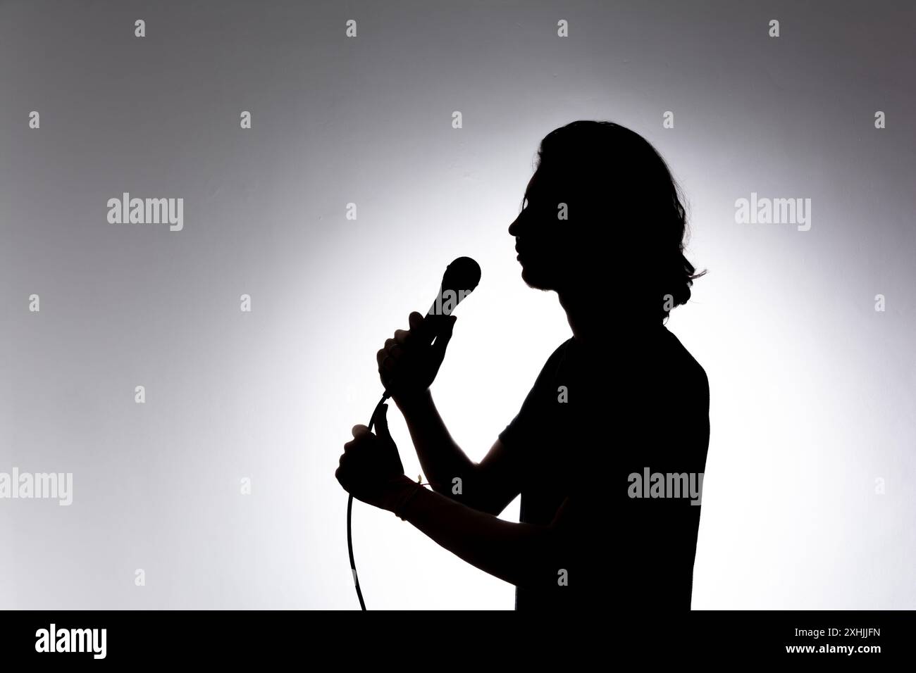 Silhouette of young singer holding wired microphone and singing with ...