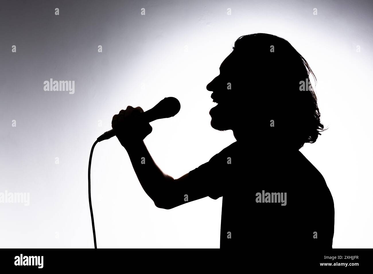 Silhouette of young singer holding wired microphone and singing with ...