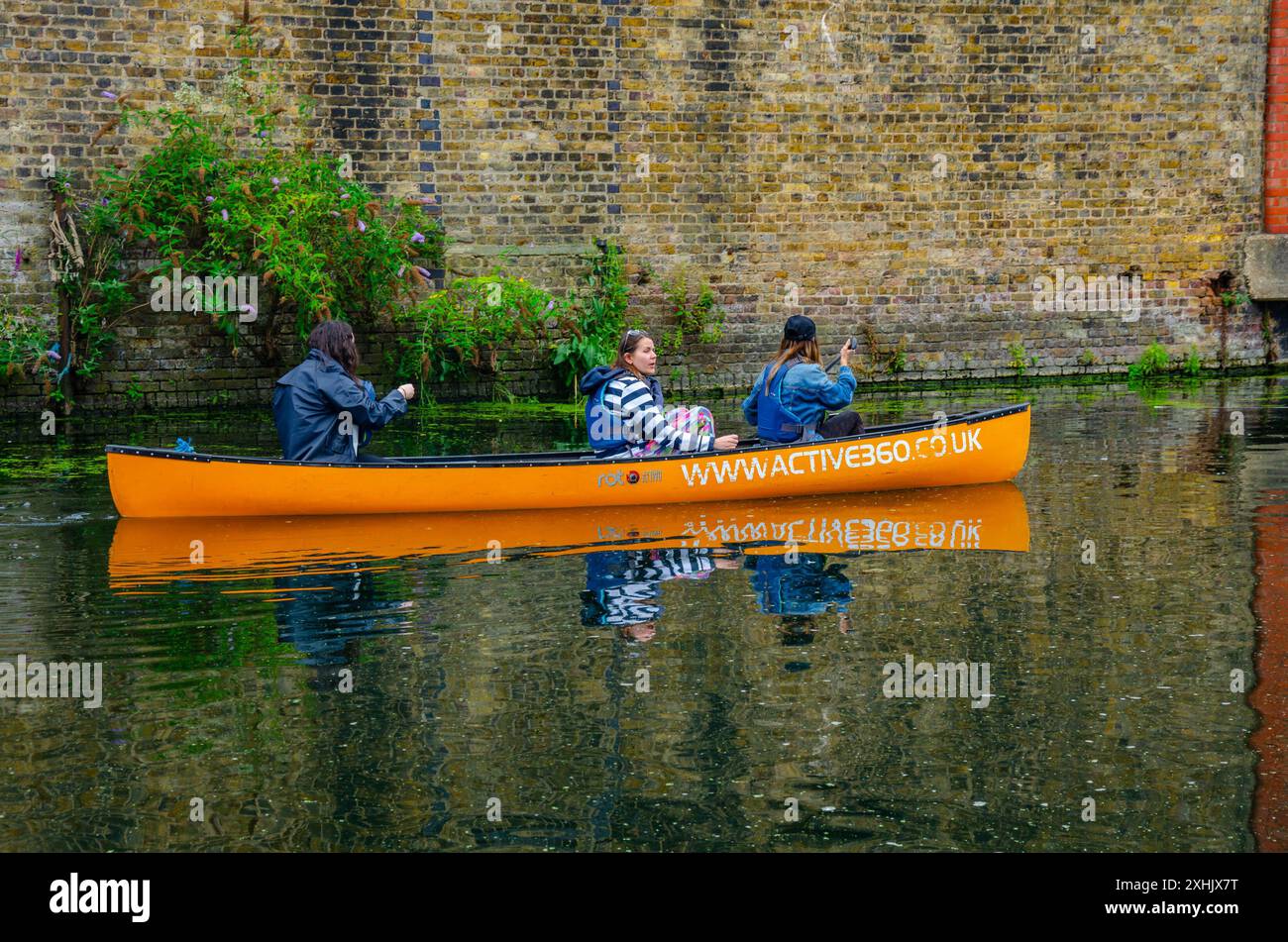 Three people paddle a canoe along the Grand Union Canal Paddington Arm ...