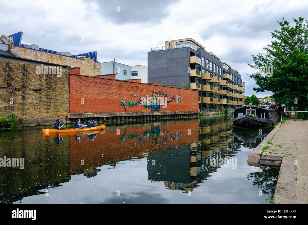Ladies in a canoe paddle past a barge moored against the bank of The ...