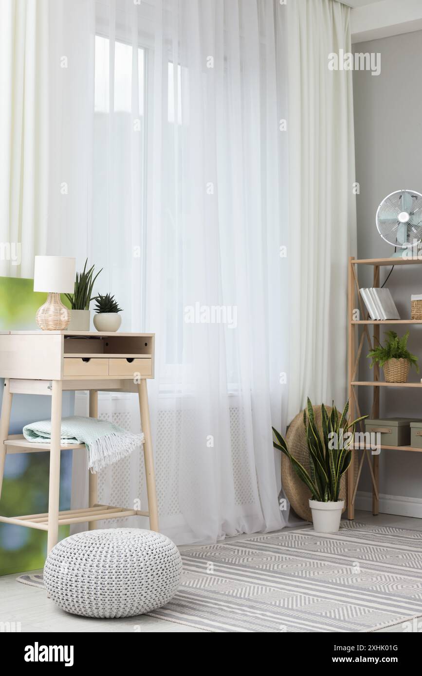 Window with beautiful curtains, pouf, houseplants and furniture in room ...