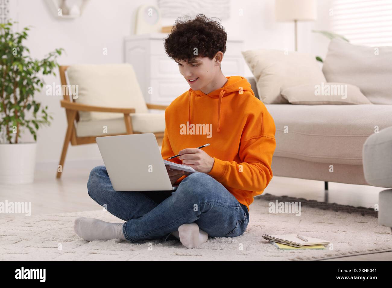 Teenager taking notes while working with laptop at home. Remote job ...