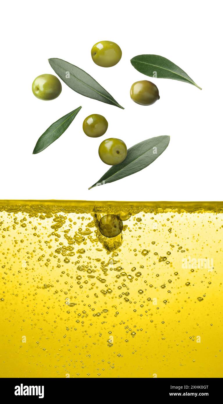 Green olives and leaves falling into cooking oil on white background ...