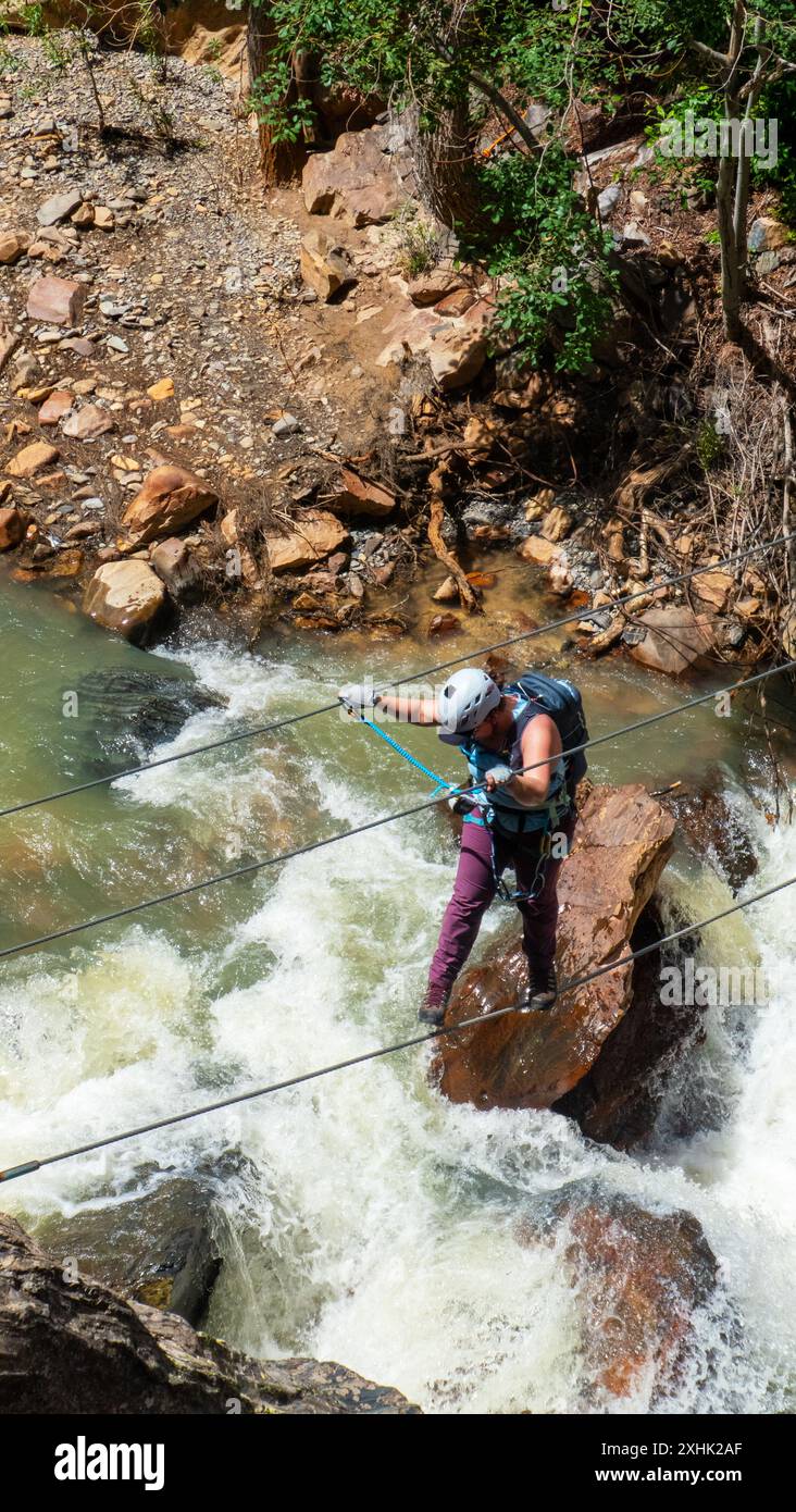 A single woman crosses a high cable above the river on via ferrata in ...