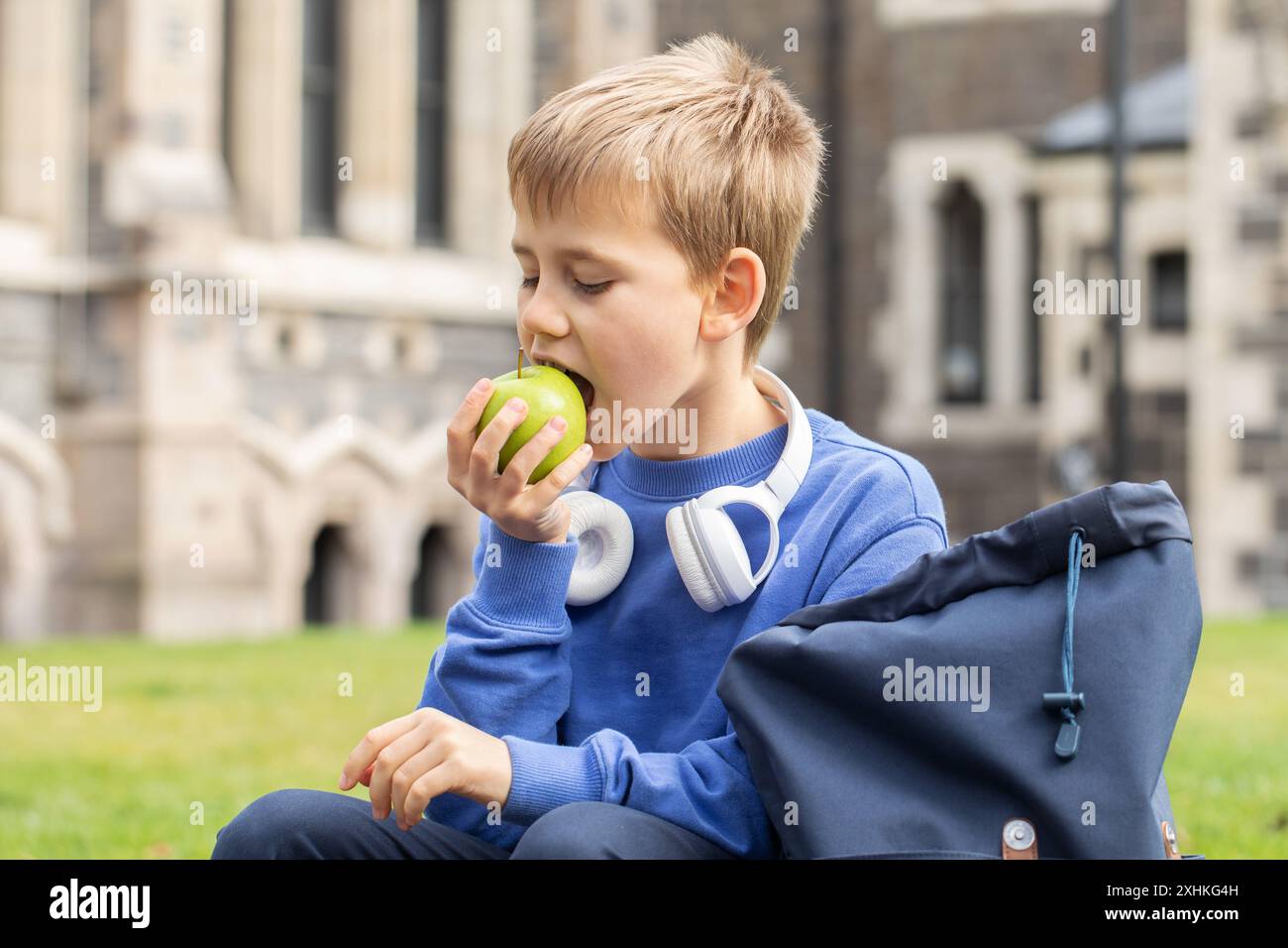 Boy student with backpack bites green apple in school yard Stock Photo ...